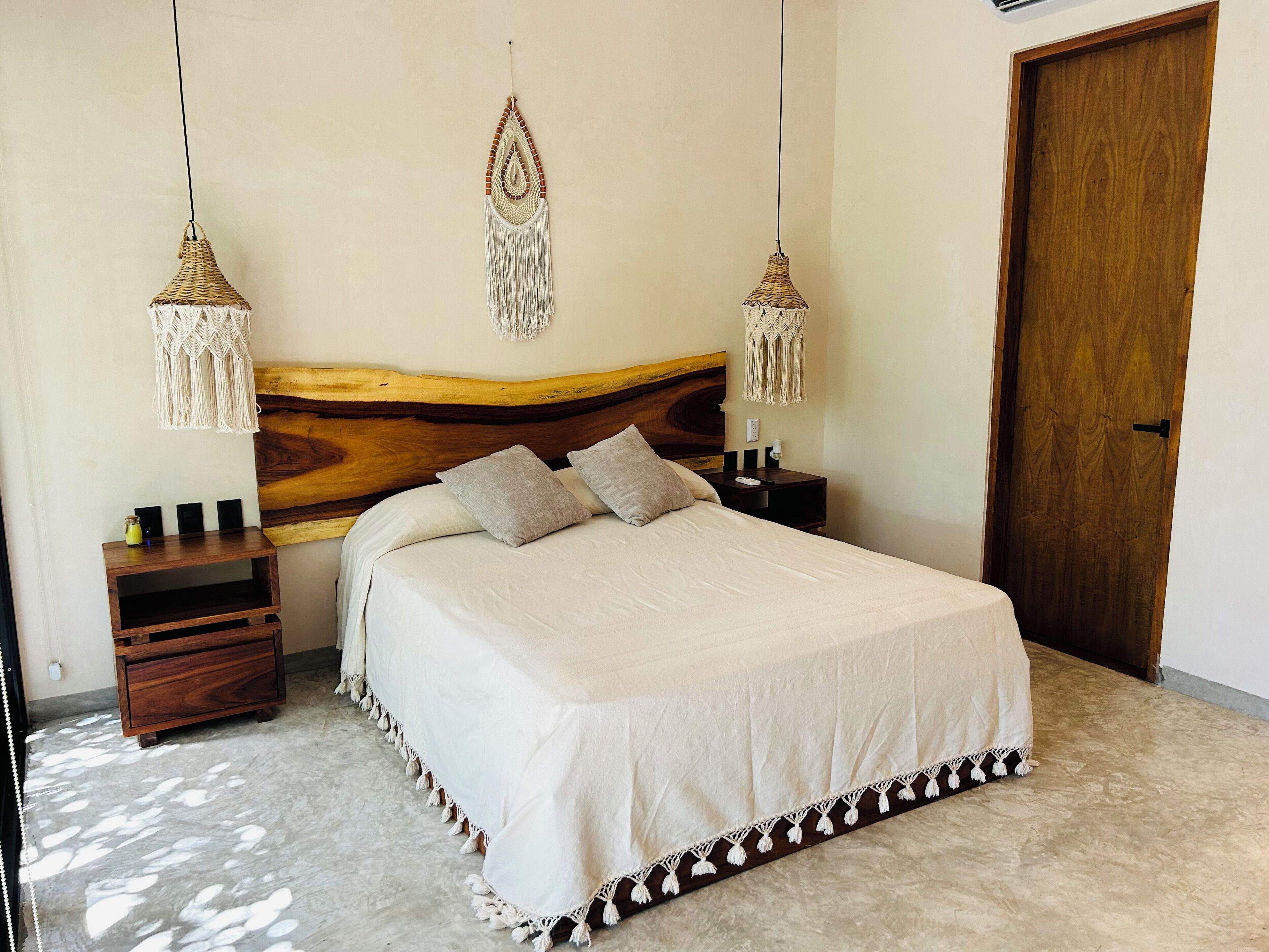 Um quarto com uma cama, duas mesinhas de cabeceira, uma cabeceira de madeira e dois painéis de macramé na parede.
