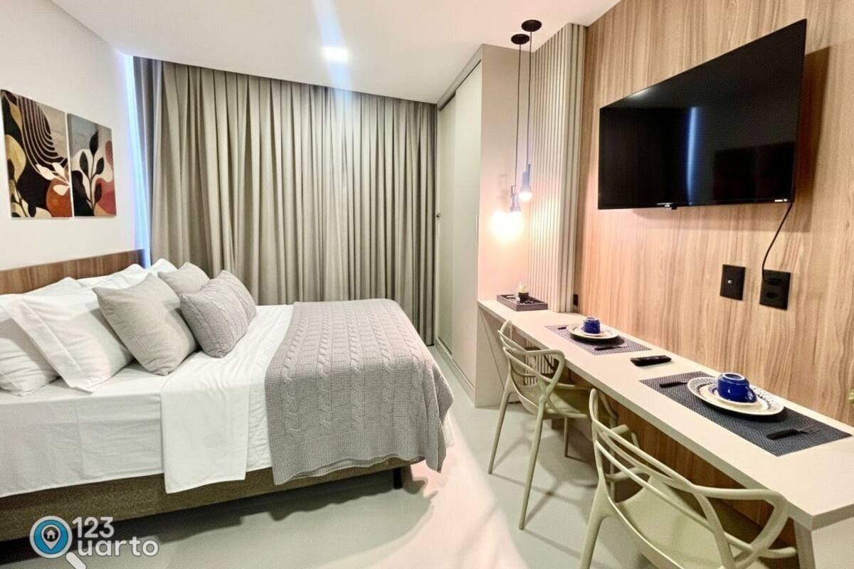 Quarto de hotel com cama, secretária com cadeiras, televisão de tela plana e cortina.
