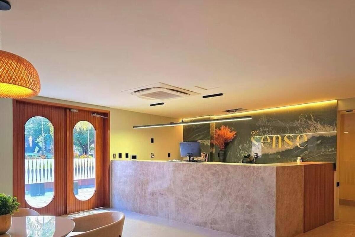 Balcão de recepção com bancada de mármore, um computador e uma parede com a palavra 'sense' parcialmente visível.