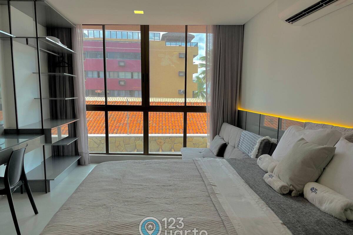 Quarto de hotel moderno com uma cama grande, uma escrivaninha e vista para um edifício com azulejos laranja.