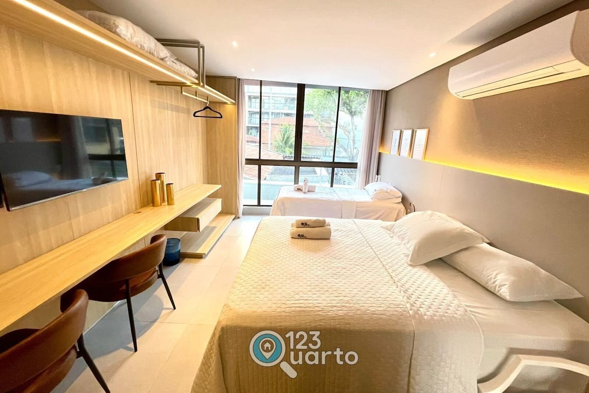 Quarto de hotel moderno com cama, escrivaninha, televisão e vista para o exterior.