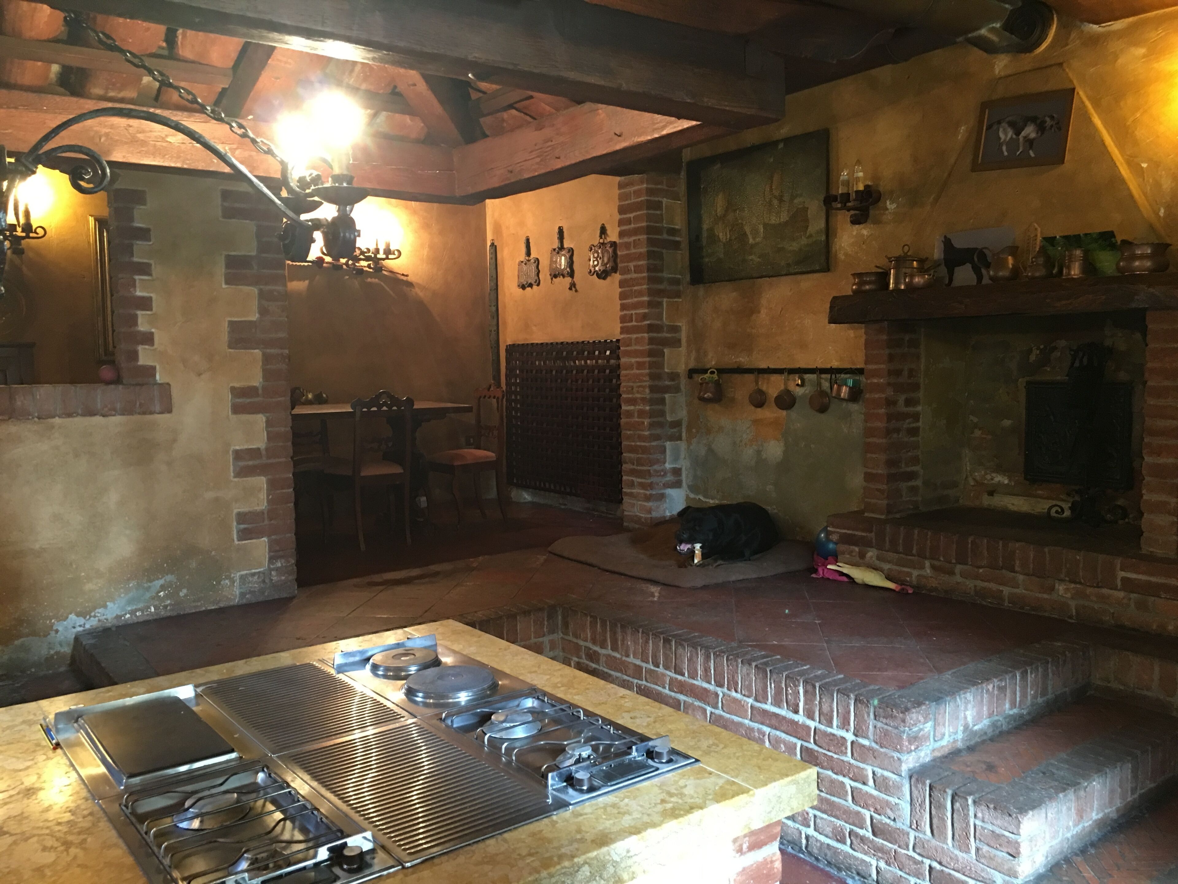 Uma cozinha rústica com lareira de tijolos, fogão a gás e área de jantar com cadeiras de madeira.