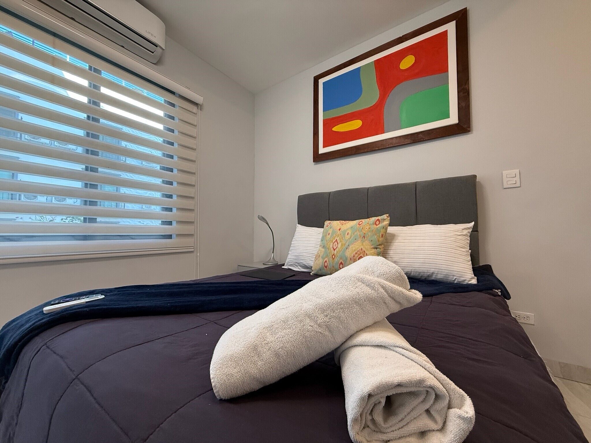Cama bem arrumada com um edredom escuro e uma toalha branca enrolada.