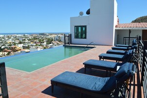 Piscina no terraço com espreguiçadeiras, vista desimpedida da cidade e um edifício moderno com antena parabólica.