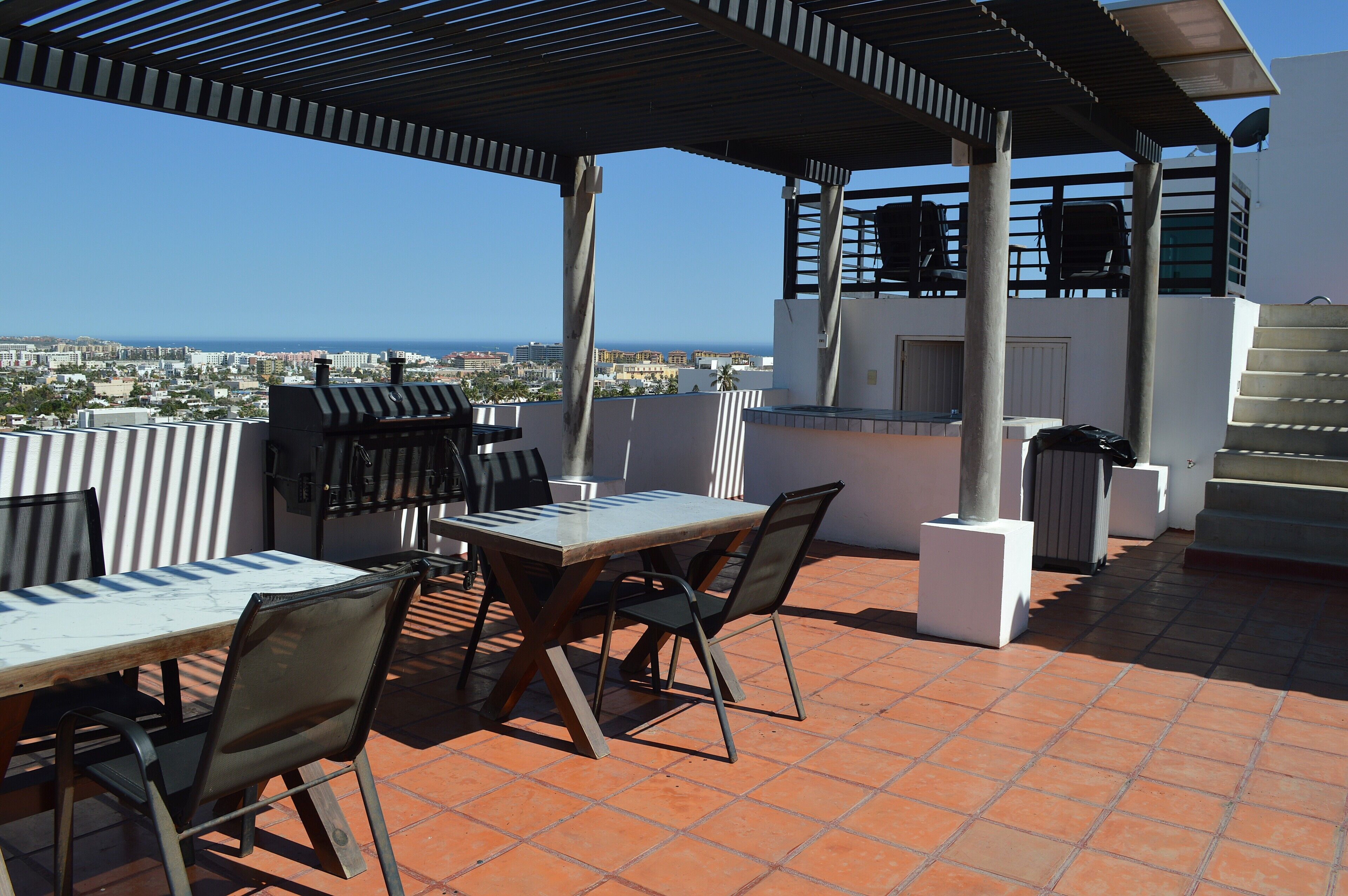 Pátio externo com mesa, cadeiras e churrasqueira, com vista para a cidade e o mar.