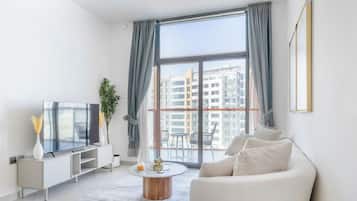 Uma sala de estar moderna com televisão de tela plana, sofá, mesa de centro e vista para a paisagem urbana através de grandes janelas.