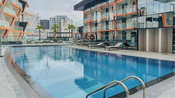 Piscina com espreguiçadeiras e edifício moderno com detalhes em laranja.