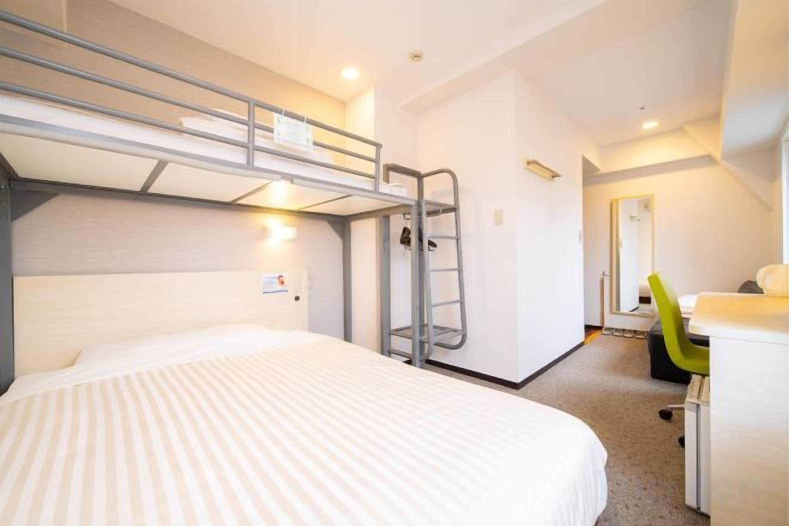 Quarto de hotel com beliche, escrivaninha e cadeira.