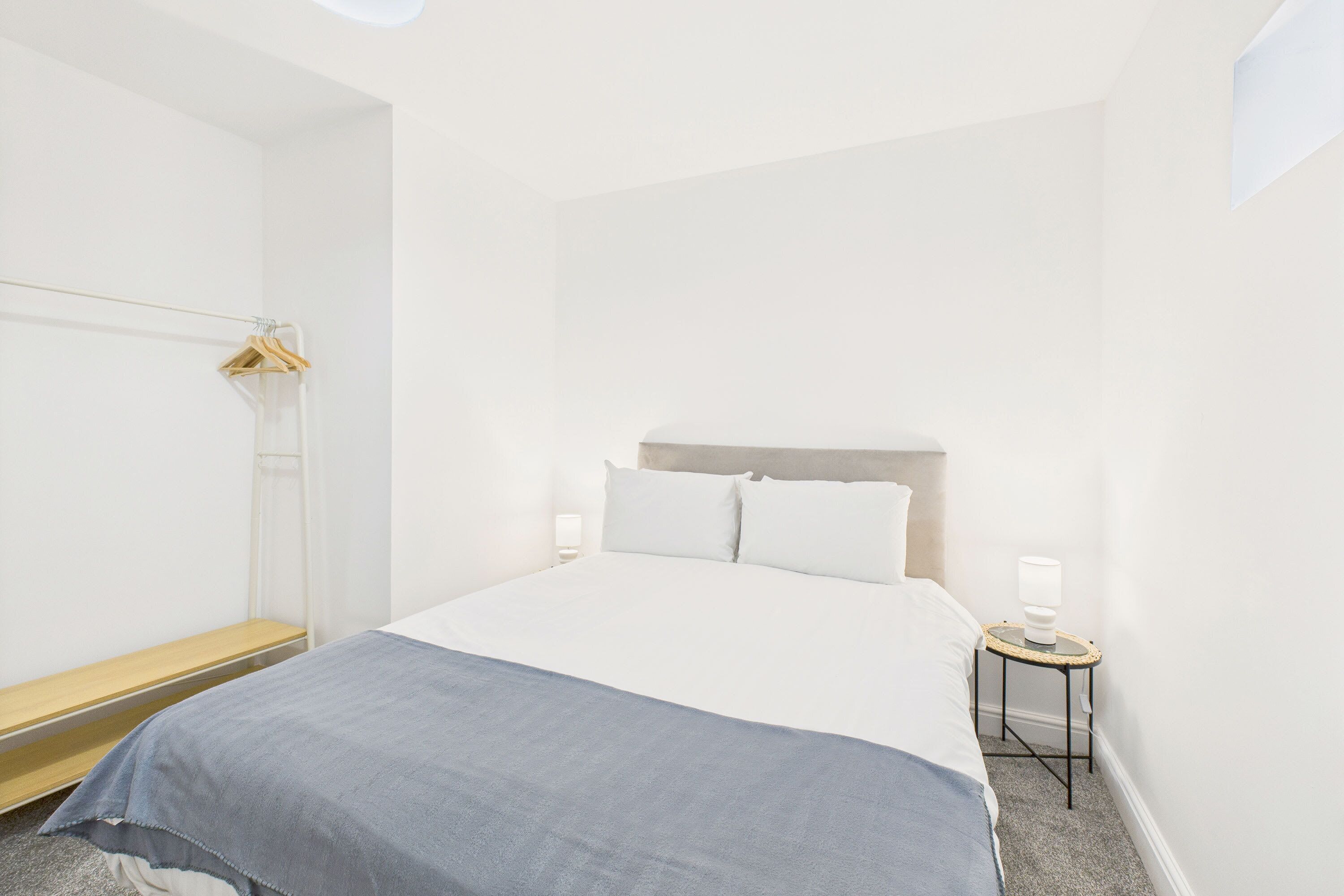 Quarto bem organizado com cama, mesa de cabeceira e um cabideiro.