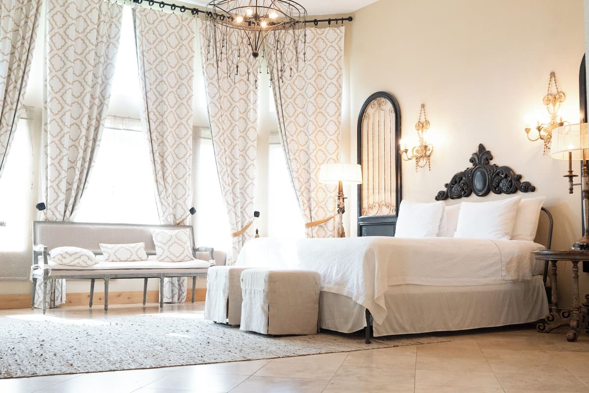 Um quarto espaçoso com uma cama grande, um espaço de estar com um banco e um espelho decorativo.
