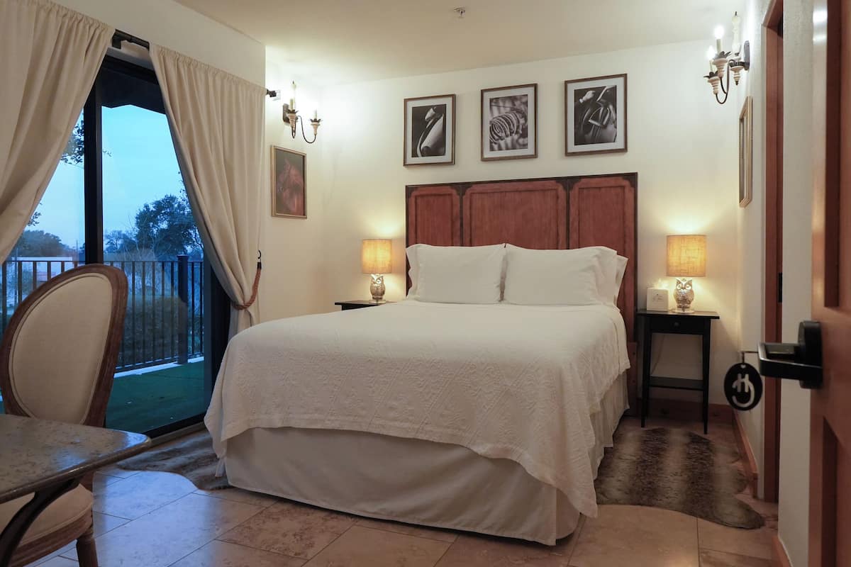 Quarto com uma cama grande, duas luminárias de cabeceira, uma poltrona e vista para o exterior por uma porta deslizante.