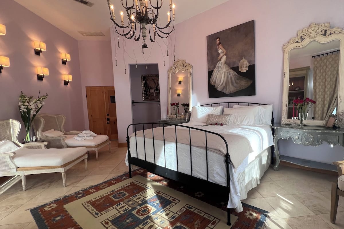 Quarto com cama, candelabro, pintura, espelho e tapete estampado.