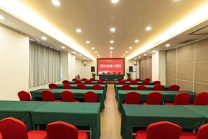 Sala de conferências com mesas e cadeiras dispostas em fileiras, uma tela de projeção e um palco na frente.