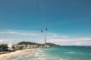Uma vila costeira com praia, um sistema de teleférico e uma colina com edifícios.