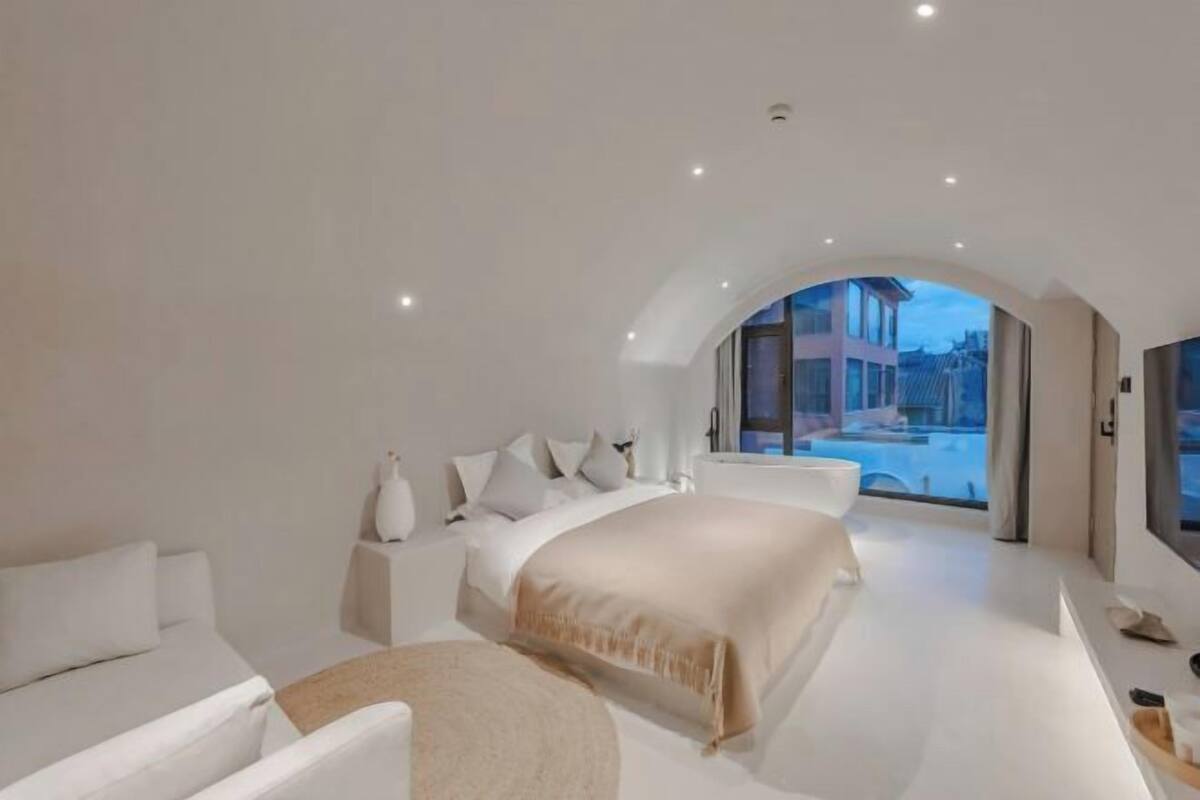 Quarto moderno com uma cama grande, um espaço de estar e vista para um edifício através de uma porta de vidro.