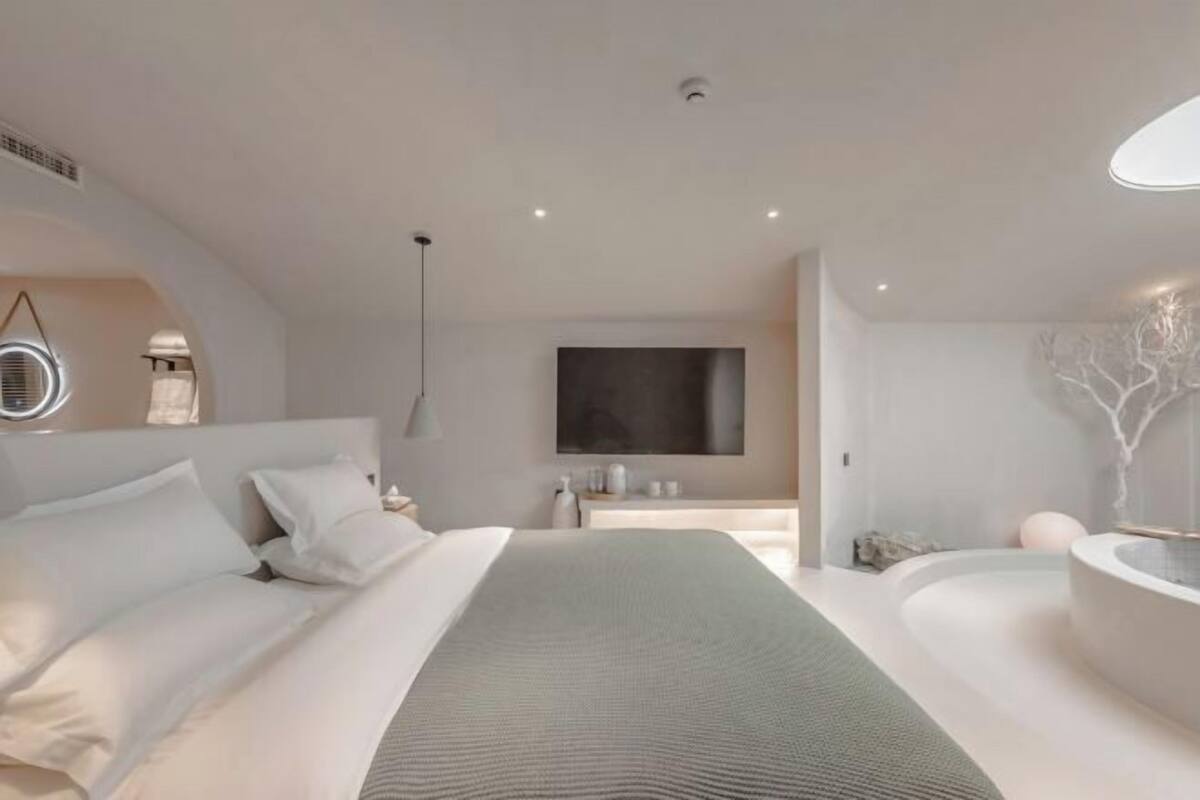 Quarto moderno com uma cama grande, uma mesinha de cabeceira, uma luminária suspensa e uma TV fixada na parede.