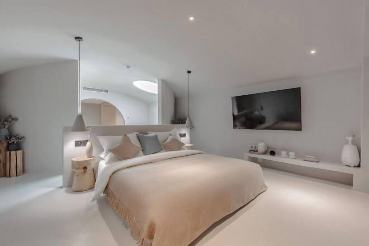 Quarto moderno com cama grande, mesa de cabeceira, televisão na parede e prateleira embutida.