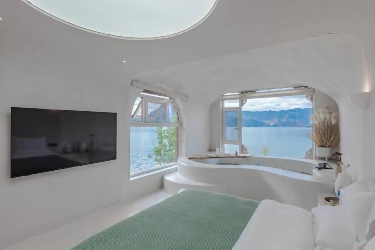 Quarto moderno com uma cama grande, uma televisão e uma banheira com vista para a água.