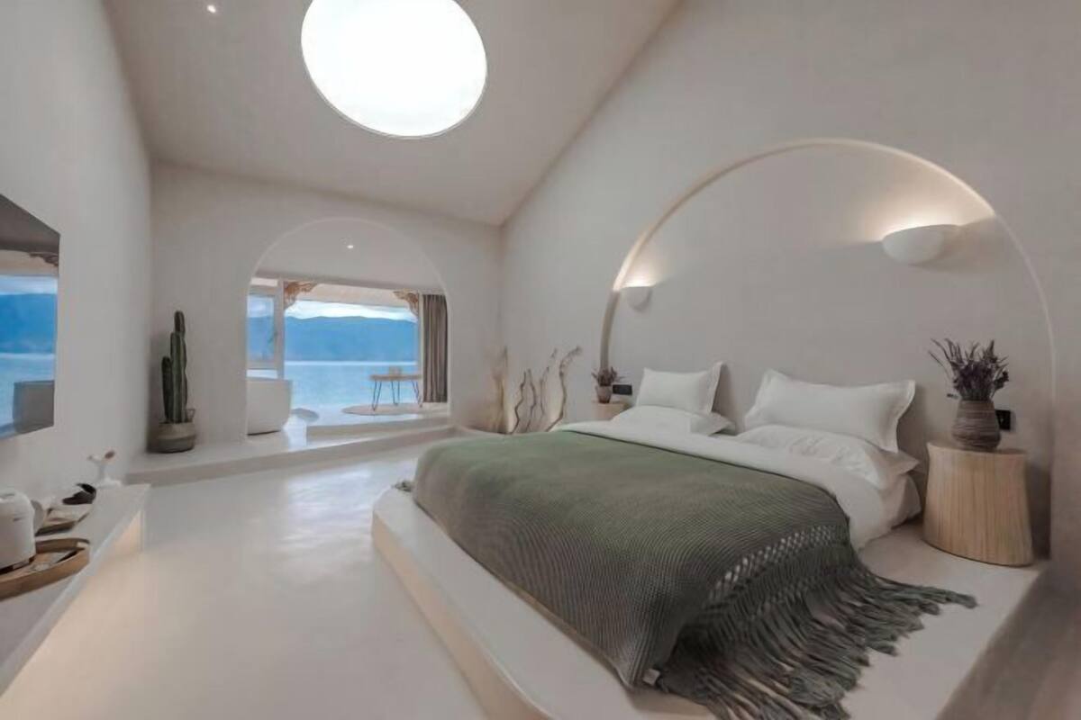Quarto moderno com uma cama grande, vista para o mar e um claraboia circular.
