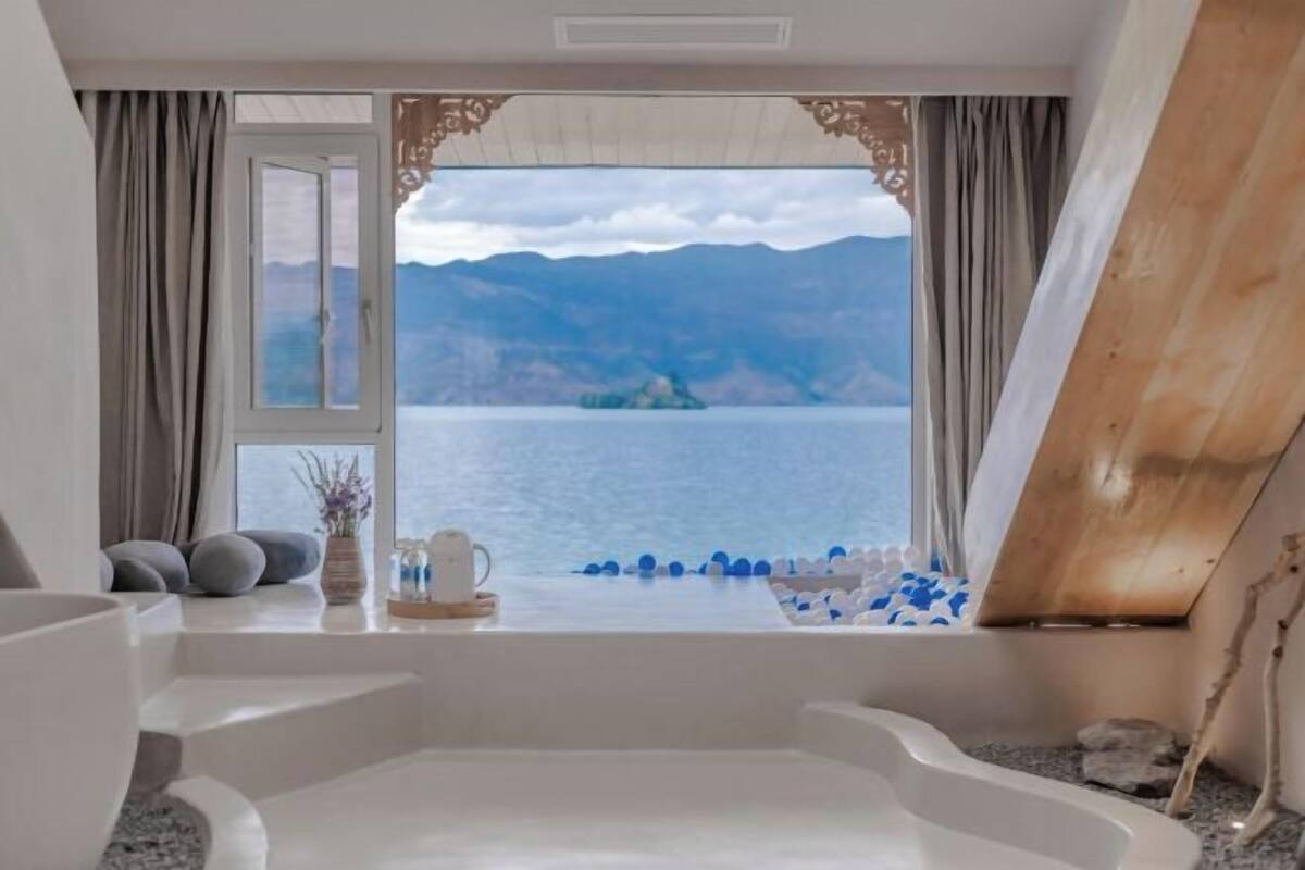Quarto com uma janela grande, uma banheira e vista para montanhas e água.
