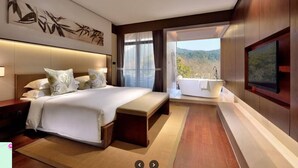 Quarto moderno com uma cama grande, um banco, uma banheira e uma televisão.