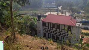 Um edifício com telhado vermelho, rodeado de vegetação e uma paisagem acidentada.