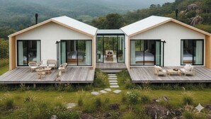 Duas cabines modernas, com paredes de vidro e varandas de madeira, com uma paisagem montanhosa ao fundo.