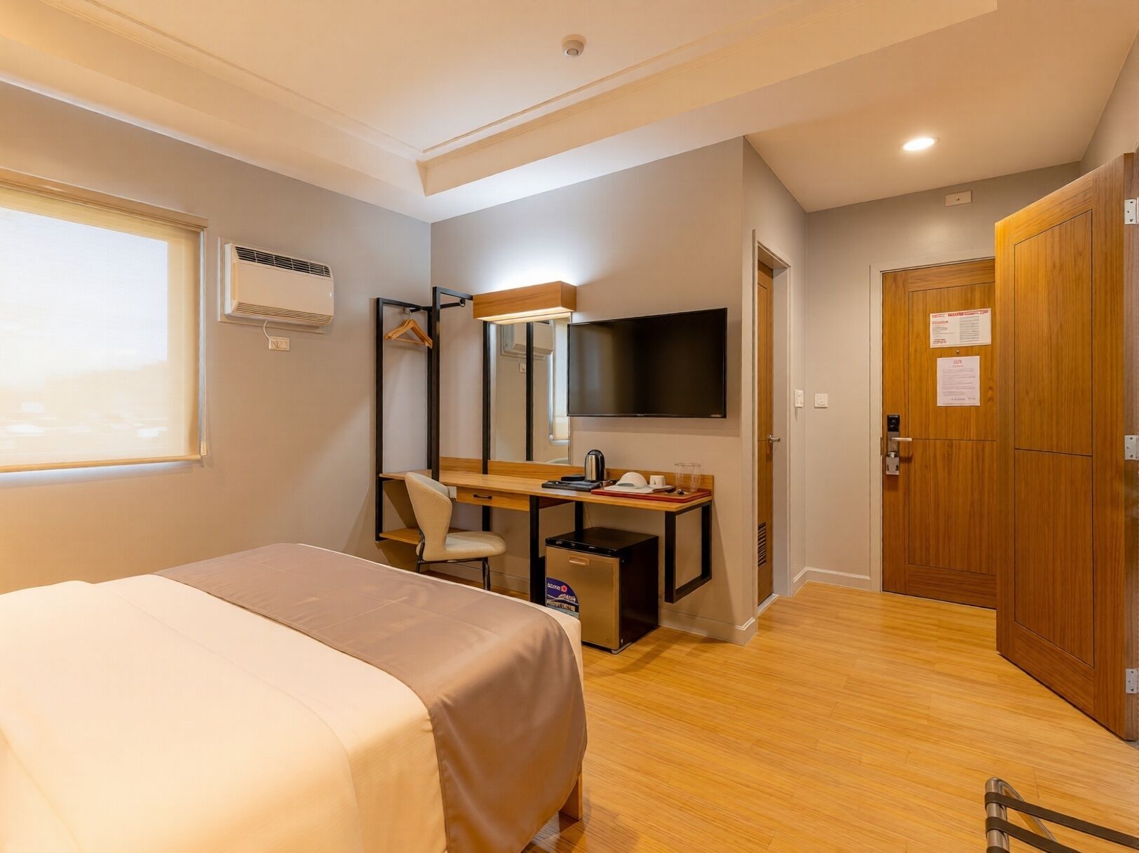 Quarto de hotel com cama, escrivaninha, cadeira, televisão e guarda-roupa.