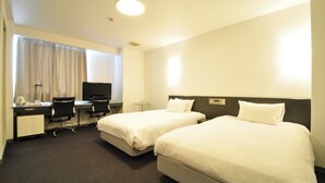 Quarto de hotel com duas camas, uma escrivaninha com cadeira, televisão e janela com cortinas.