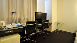 Quarto de hotel com uma escrivaninha, duas cadeiras de escritório pretas, uma televisão, um telefone, um copo e uma mesa pequena.