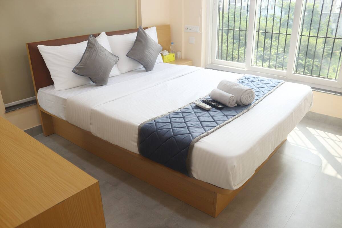 Cama bem arrumada com manta acolchoada, travesseiros e toalha enrolada.