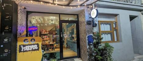 Fachada com porta de vidro, letreiro neon e pequena área externa com plantas.