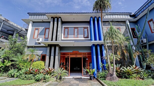 Um edifício moderno com entrada de vidro, rodeado por plantas tropicais e um caminho de cascalho.