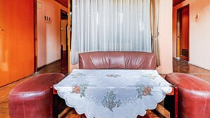 Um quarto com um banco de madeira, uma mesa com toalha de mesa florida e uma cortina.