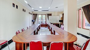 Uma sala de conferências com uma mesa de madeira comprida, cadeiras vermelhas e um quadro branco.