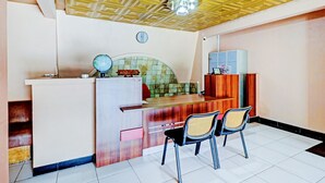 Uma área de recepção com balcão de madeira, duas cadeiras, um relógio e piso de azulejos.