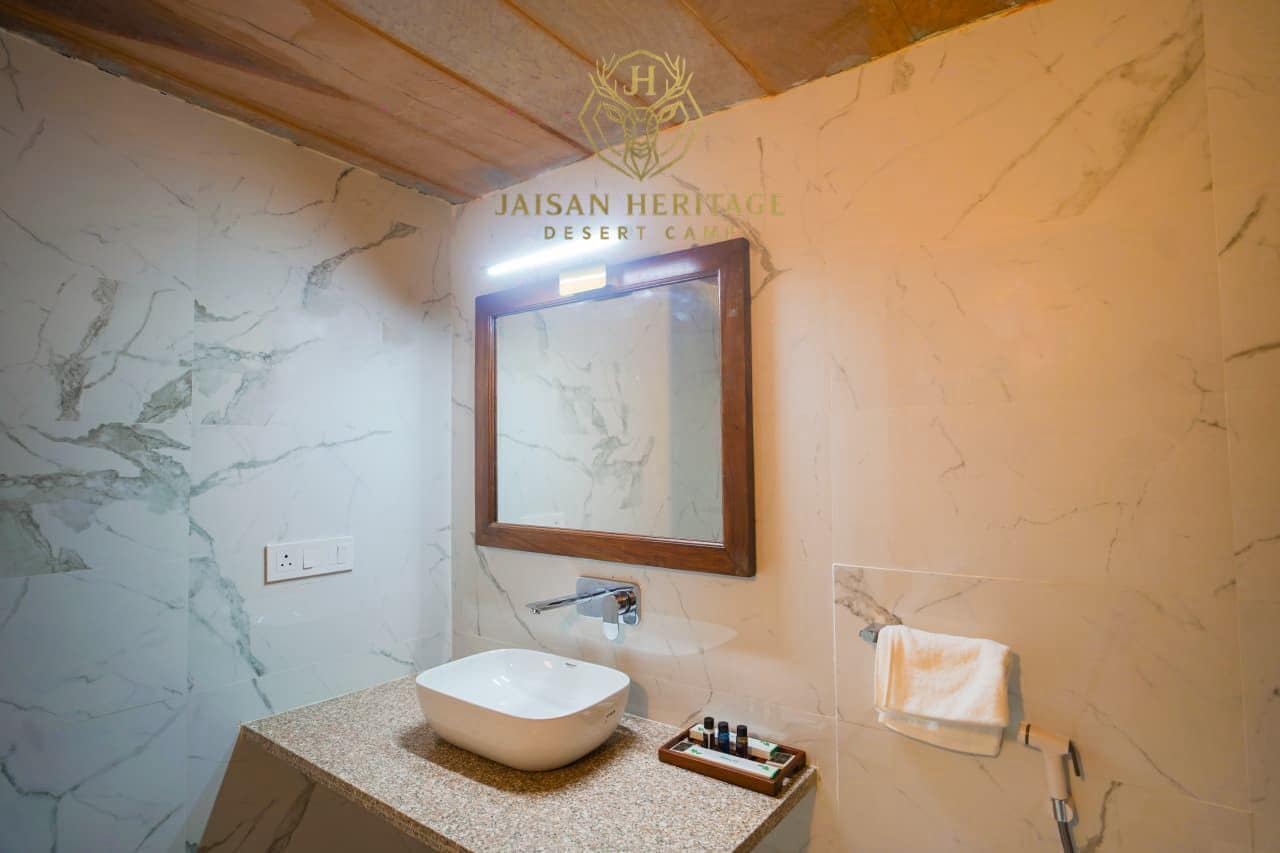 Casa de banho com parede de mármore, lavatório branco, espelho e porta-toalhas.