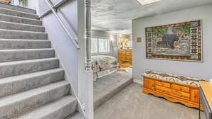 Uma escada leva a um quarto com cama, cômoda e um quadro na parede.