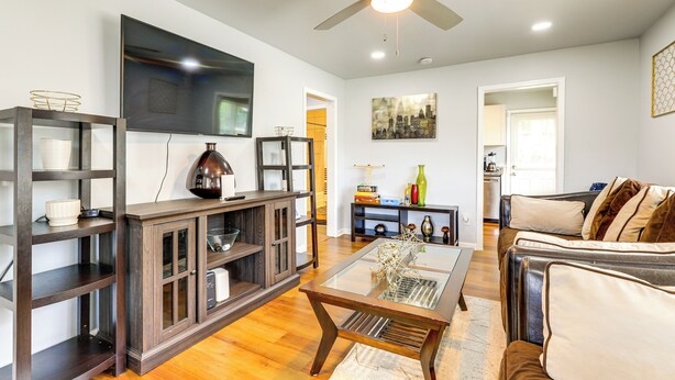 Uma sala de estar moderna com uma mesa de centro de vidro, estantes de madeira escura, uma TV de tela plana e um ventilador de teto.