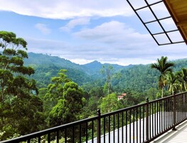 Uma varanda com vista para montanhas verdes exuberantes e um prédio de telhado vermelho ao longe.