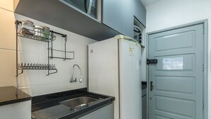 Cozinha compacta com pia, geladeira e porta com um aviso.