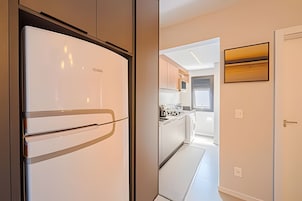 Cozinha moderna com geladeira branca, armários de madeira e vista para a sala de jantar.