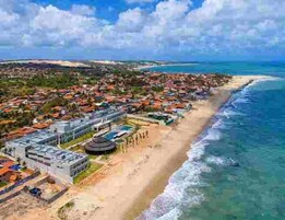 Vista aérea de um resort costeiro com praia, um grande edifício de hotel e área de piscina.