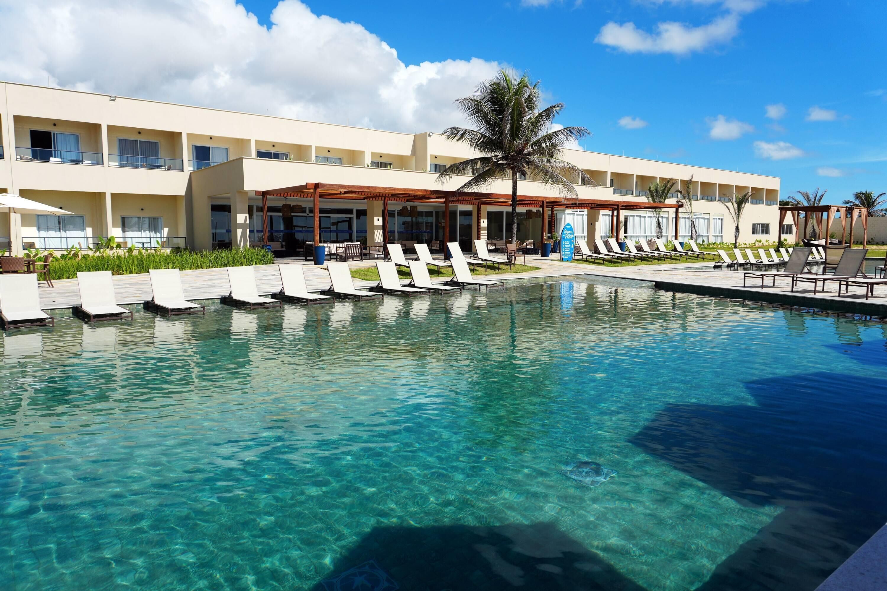 Um hotel com piscina, espreguiçadeiras e uma palmeira.