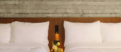 Quarto de hotel com duas camas, cabeceira de madeira, mesa de cabeceira com um vaso de flores e parede com textura.