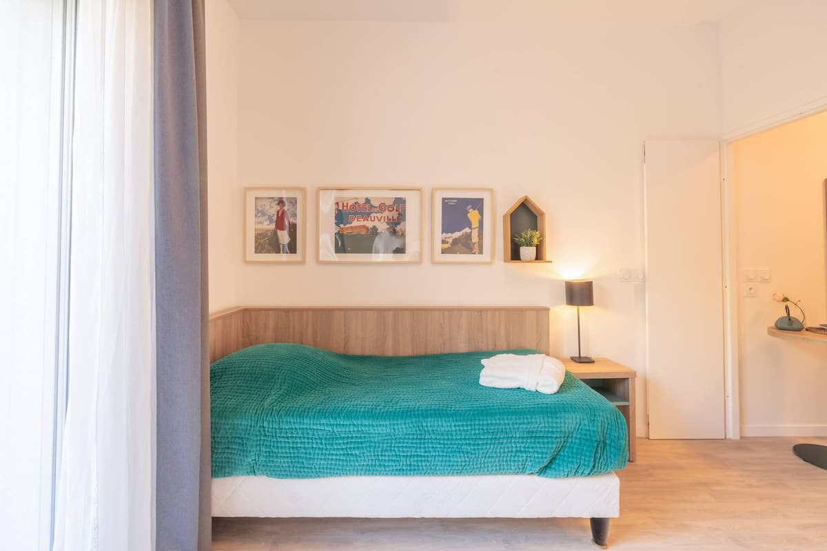 Uma cama bem arrumada com um cobertor verde, uma luminária de cabeceira e três quadros na parede.