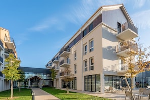 Um edifício moderno de vários andares com varandas, entrada coberta e área de estar ao ar livre.