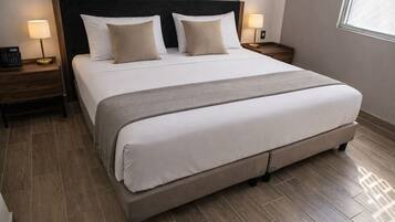 Uma cama grande com cabeceira, duas mesas de cabeceira com abajures e uma janela com persianas.