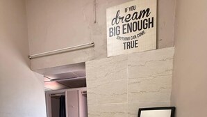 Um corredor com um espelho, uma frase motivacional e uma porta que dá para outro quarto.