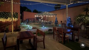Uma área de pátio ao ar livre com mesas e cadeiras, luzes de cordão e um pinheiro de Natal.